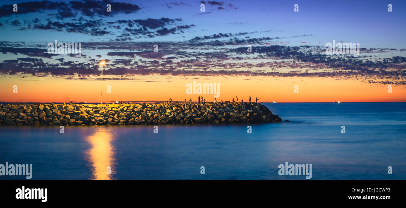 Distant view of men fishing on a jetty at sunset, Cottesloe, Perth ...