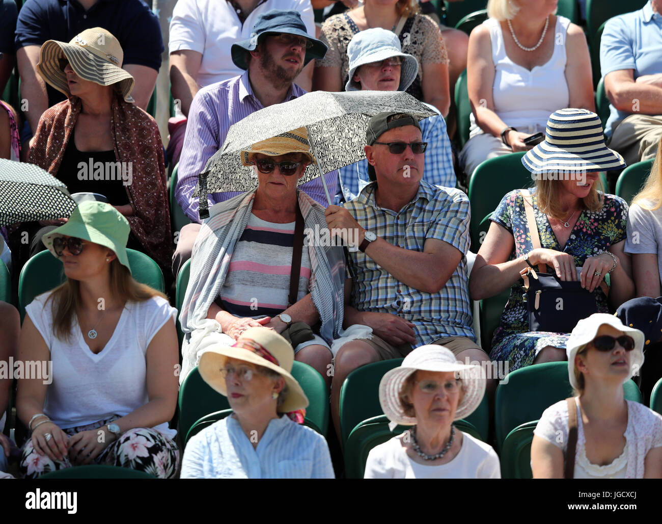 Spectators shield from the sun under umbrella's and sun hats on day ...