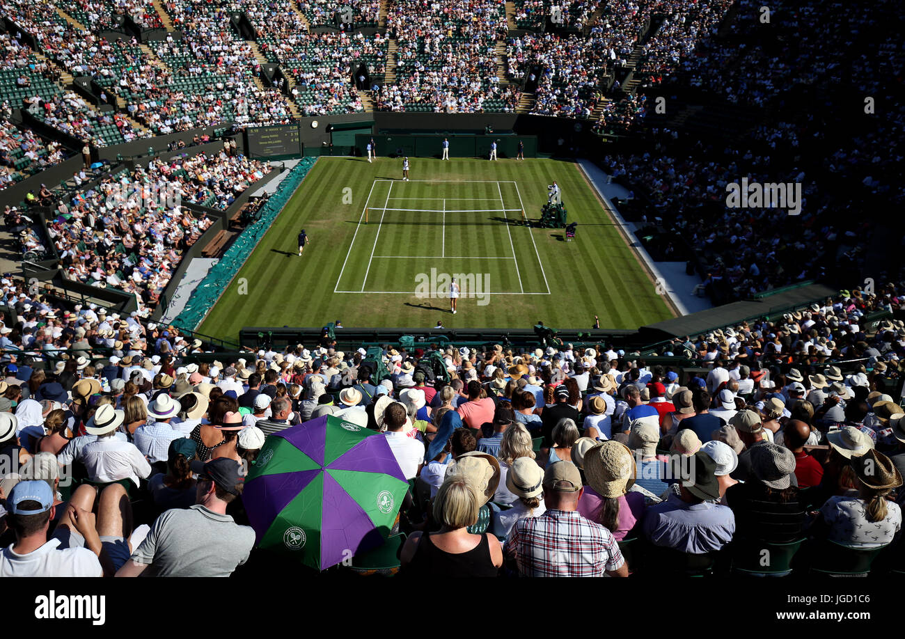 A spectator shelters from the sun under a Wimbledon umbrella as they ...