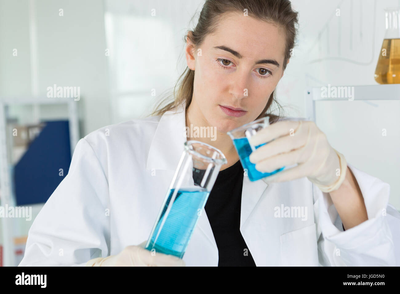 female scientist putting blue liquid into the flask Stock Photo - Alamy