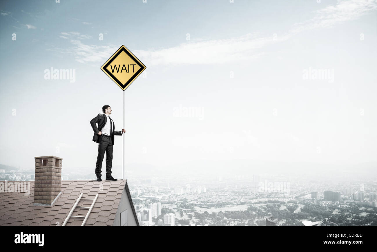 Young businessman on house brick roof holding yellow signboard a Stock ...
