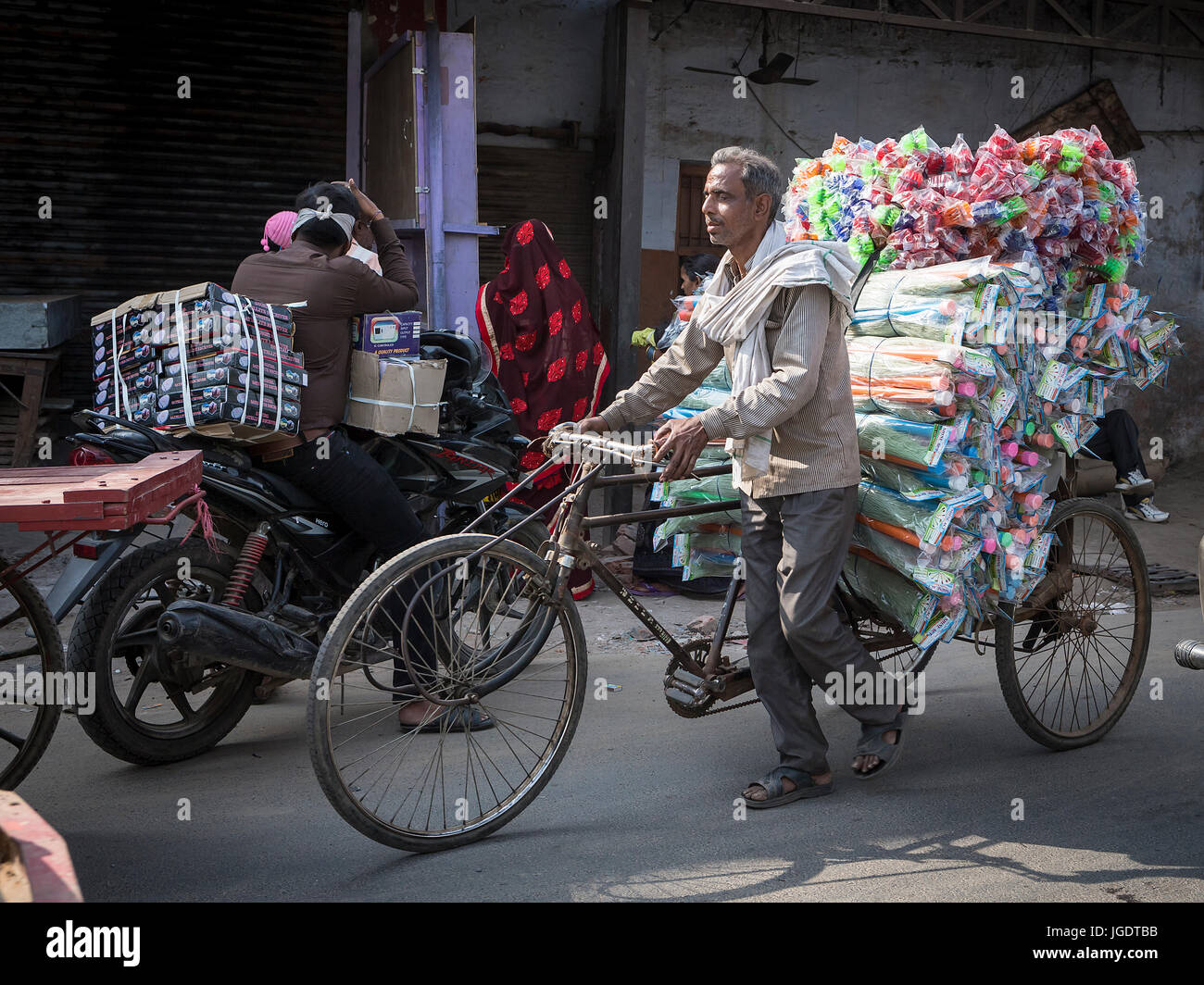 Indian man with tricycle overloaded with packets of brushes and brooms ...