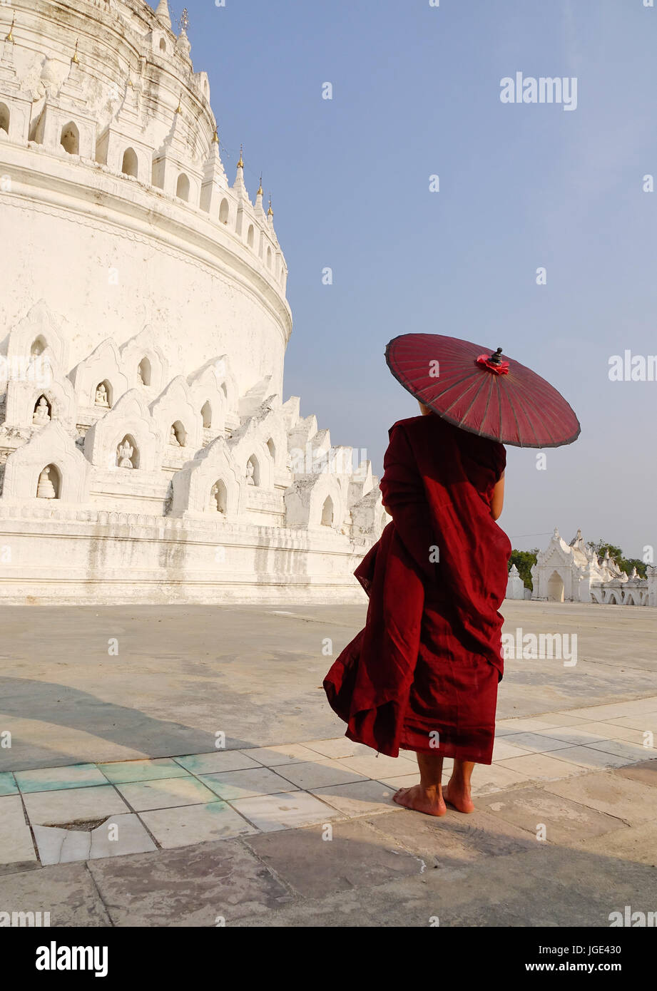 A Buddhist monk in the red robe with umbrella at the acient pagoda ...