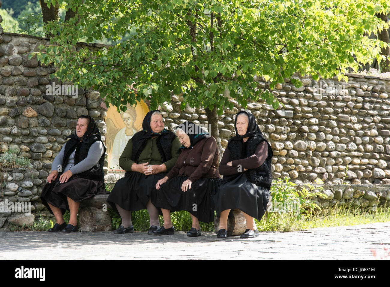Five senior people sitting on a wooden bench on a small country road in ...