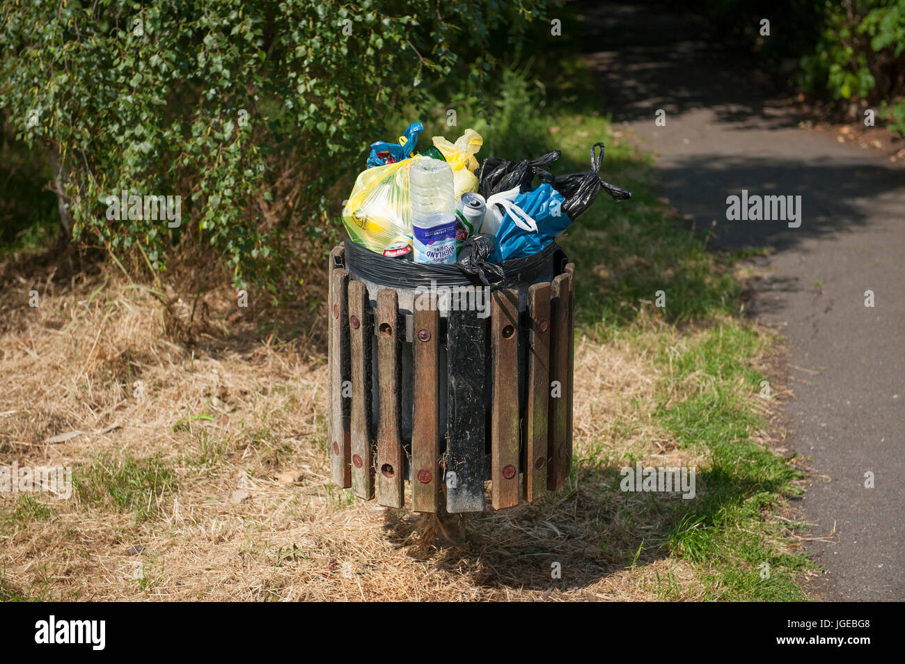 Litter bin filled with trash beside footpath Stock Photo - Alamy