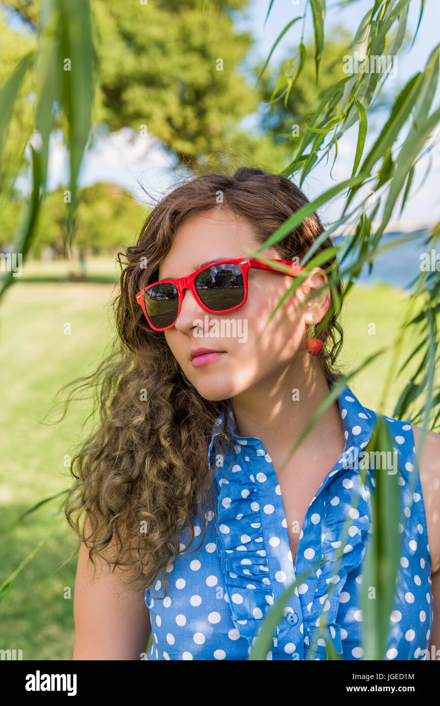 Portrait of young woman in red sunglasses standing under willow tree ...