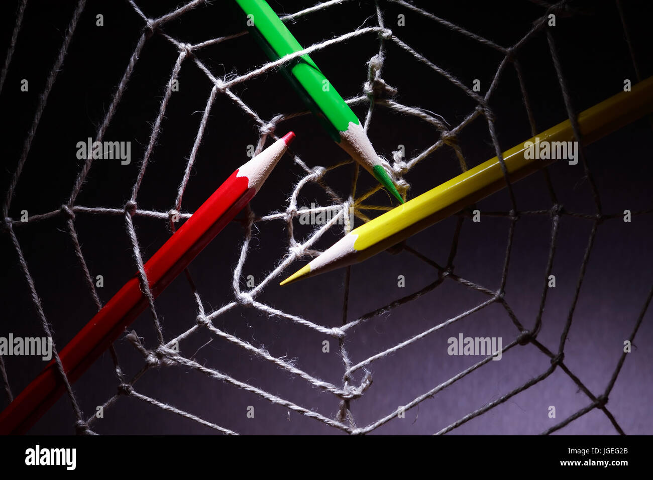Web design concept. Three color pencils in rope web on dark background ...