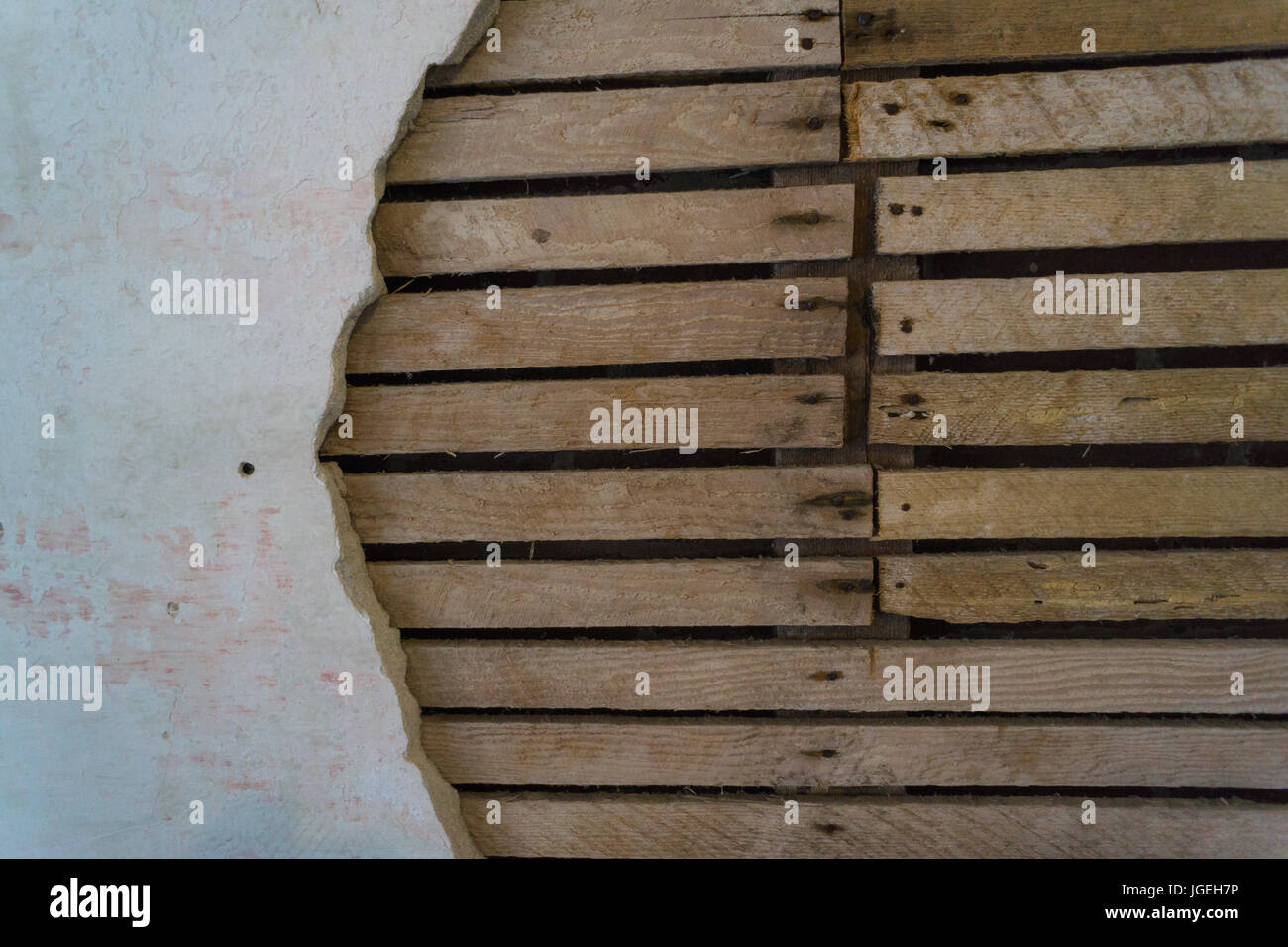 Damaged wall with broken drywall and exposed slats and timber ...