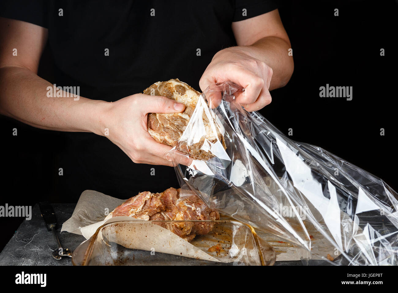 Man packs marinated pieces of meat of pork shoulder in roasting sleeve ...