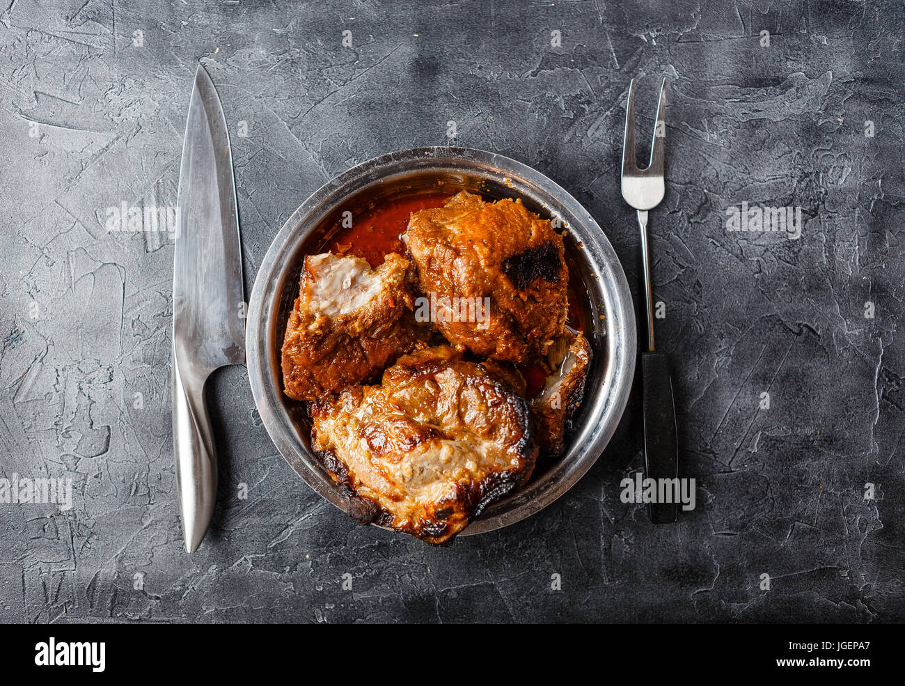 Roasted pork shoulder blade in metal plate and meat fork with knife on ...