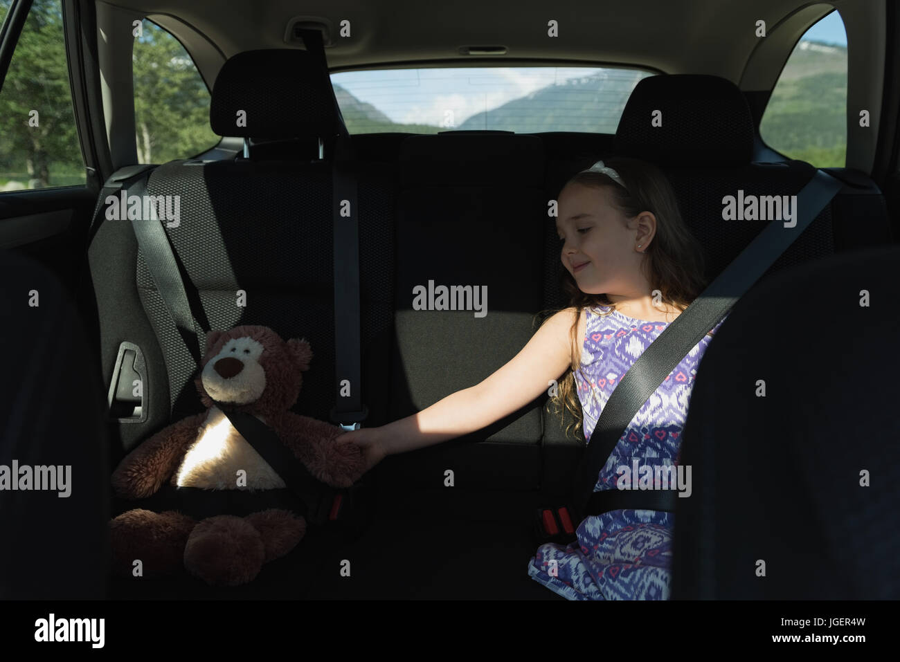 Cute girl sitting with teddy bear in car back seat Stock Photo - Alamy