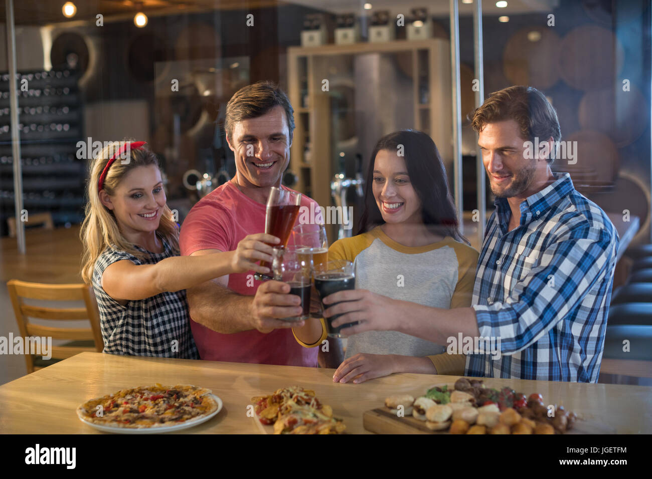 Happy friends toasting beer while standing at table in bar Stock Photo ...