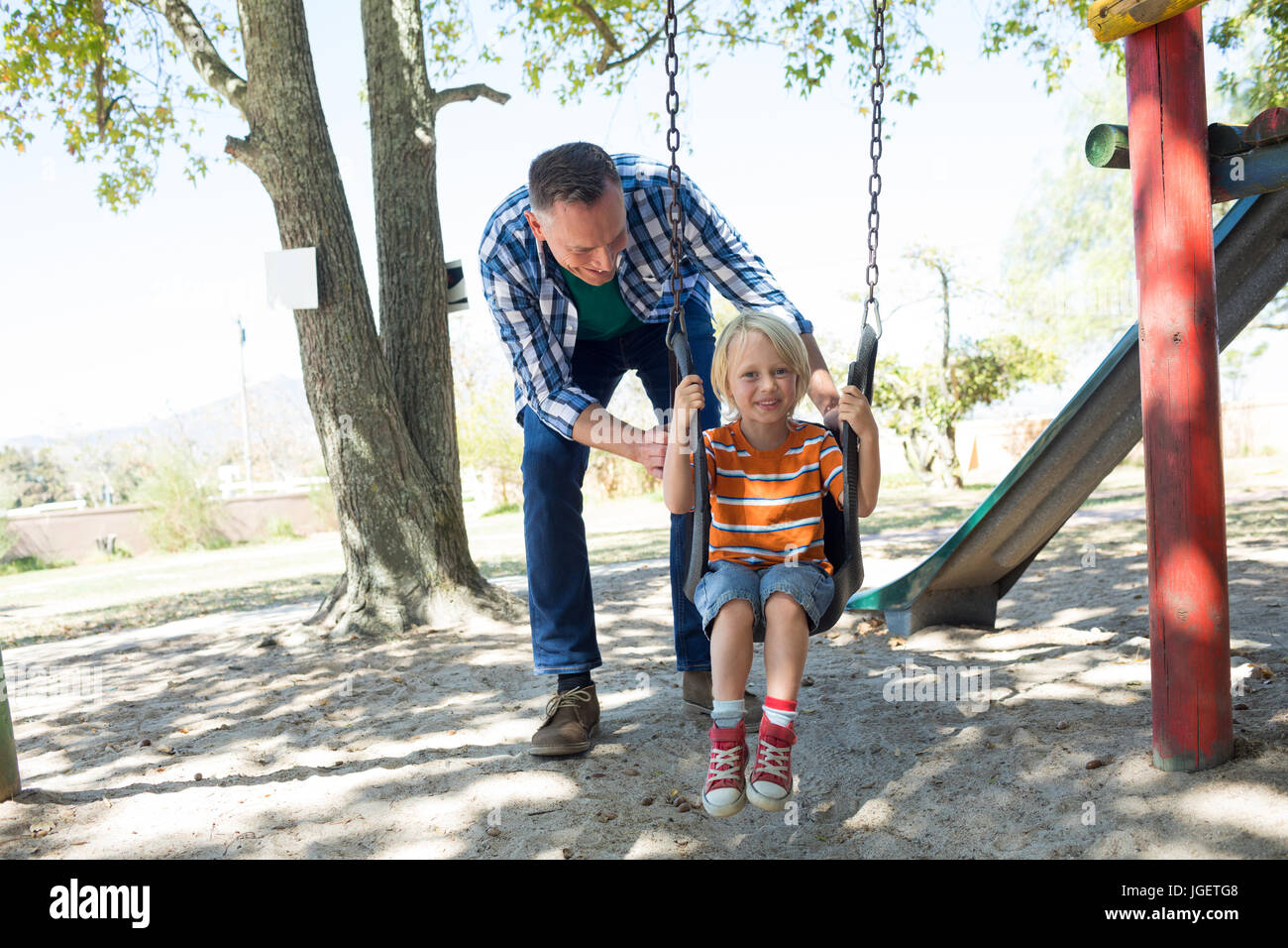 Father pushing son sitting on swing at playground Stock Photo - Alamy