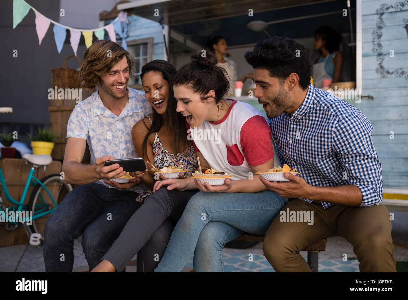 Happy friends using mobile phone while having snacks Stock Photo - Alamy