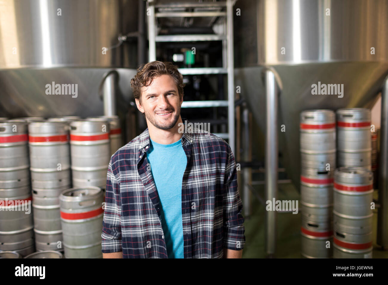Portrait of smiling male worker standing by storage tanks at factory ...