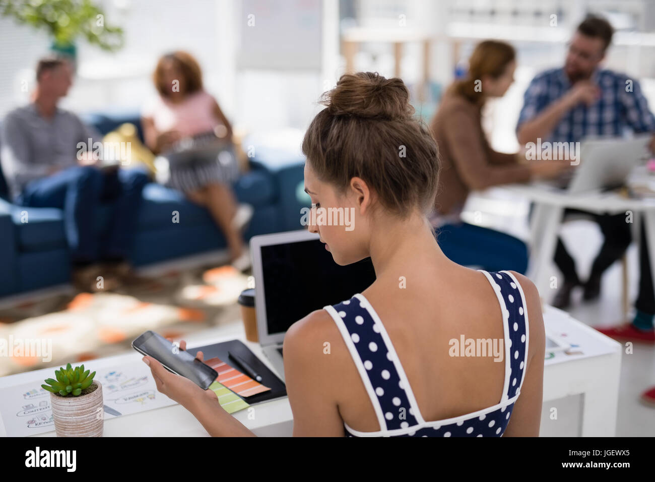 Female executive using mobile phone while working at desk in the office ...