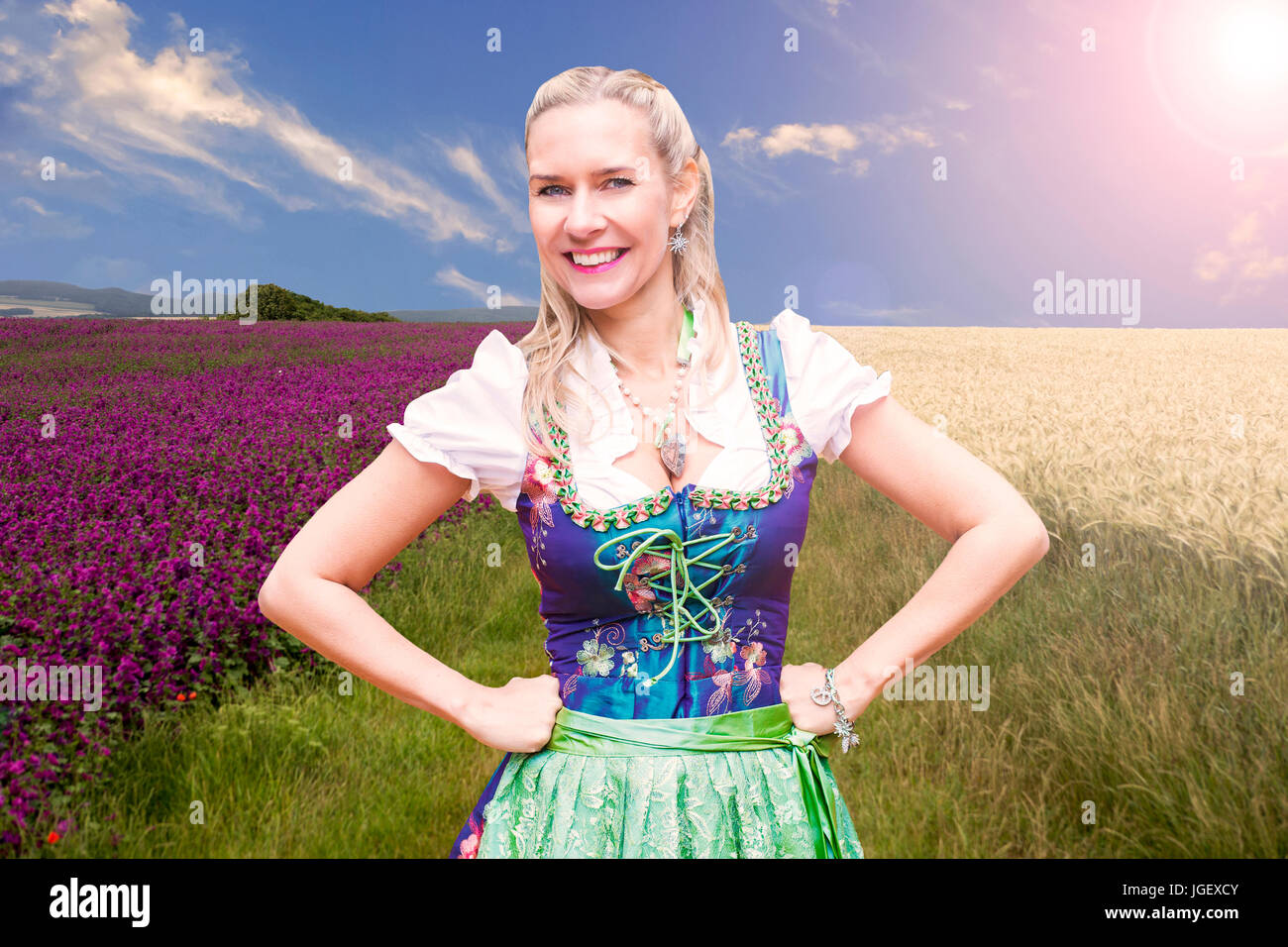 portrait of blonde woman in dirndl standing in front of flower field ...