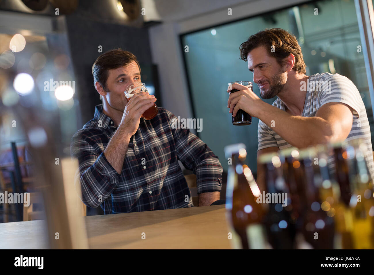 Male friends drinking beer while sitting at bar counter Stock Photo - Alamy
