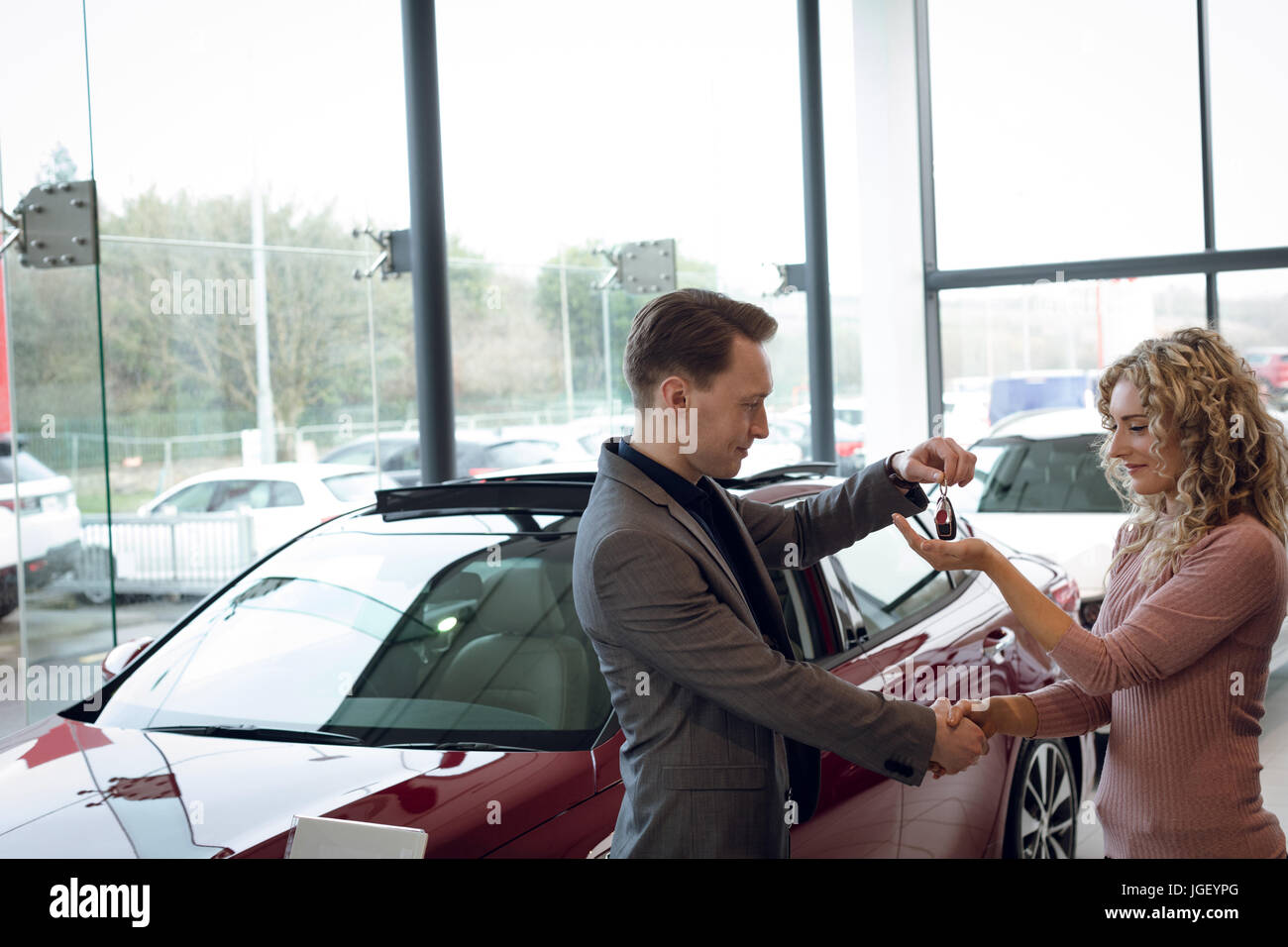 Salesman doing handshake while giving keys to customer Stock Photo - Alamy