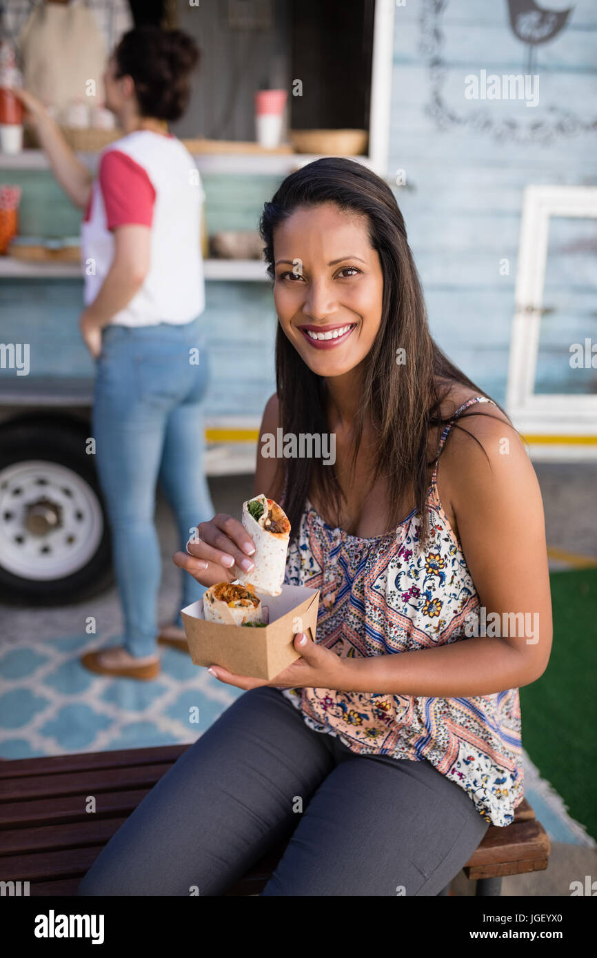 Portrait of woman sitting on bench and eating wrap Stock Photo - Alamy