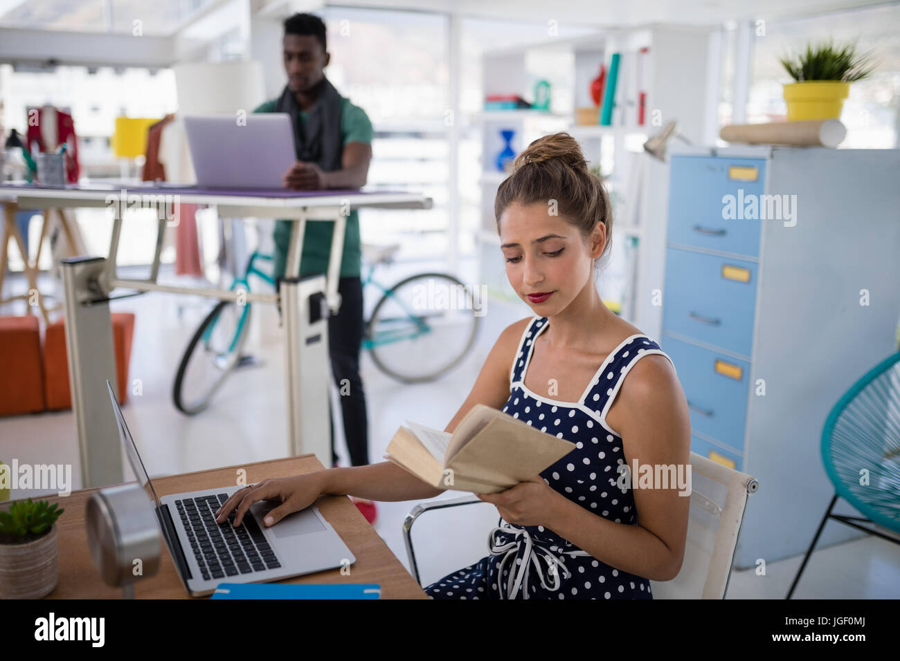 Female executive working on laptop while reading a book at desk in the ...