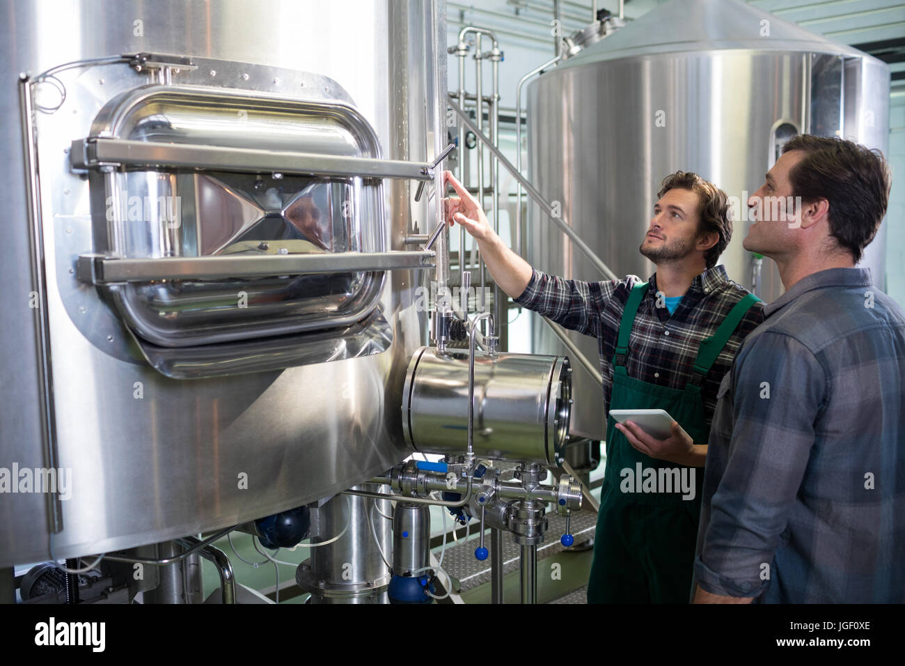 Worker holding digital tablet explaining to coworker at factory Stock ...