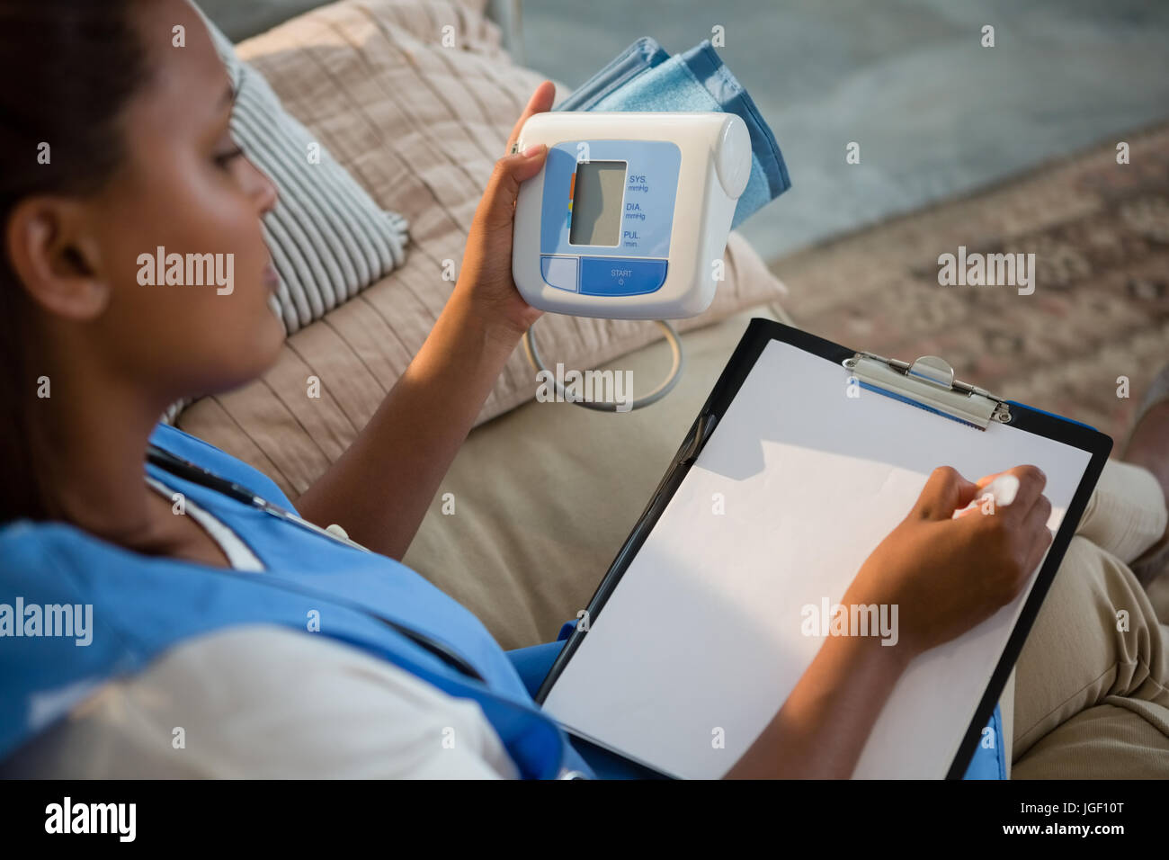 Doctor holding blood pressure monitor and writing on clipboard in ...