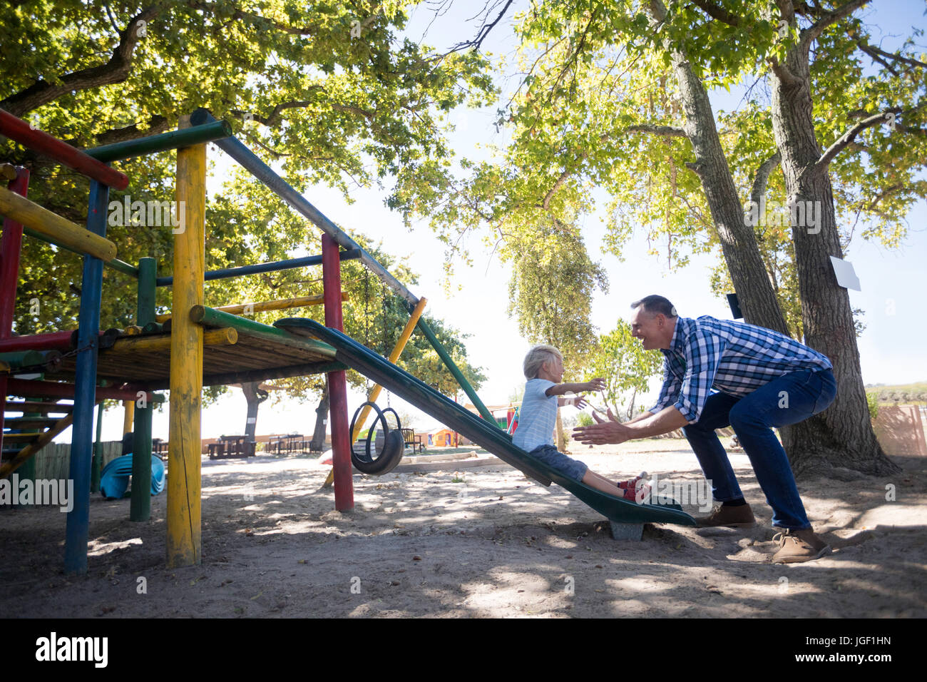 Side view of father looking at son sliding at playground Stock Photo ...