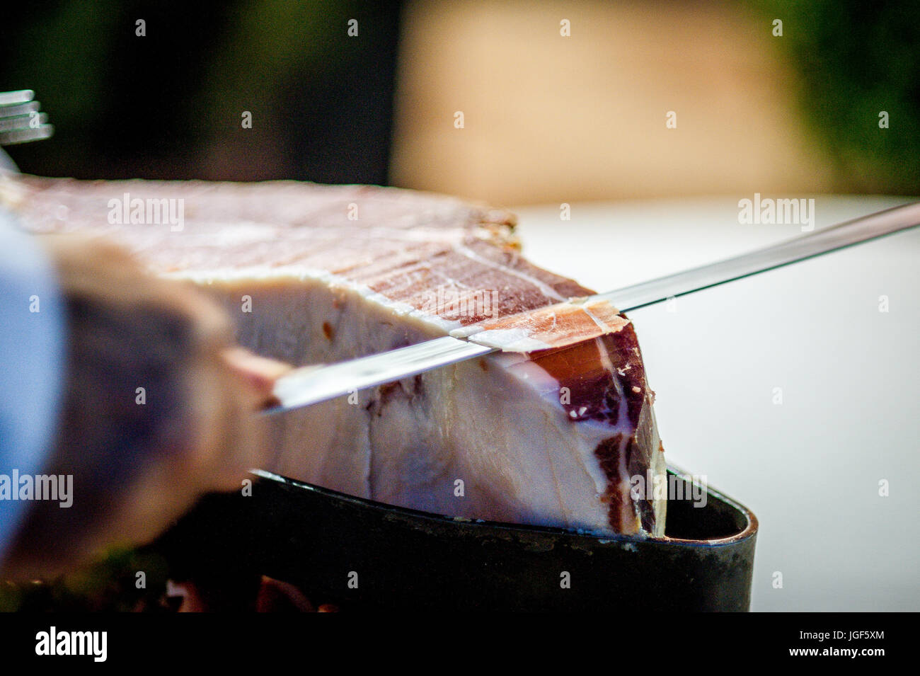 Human hand cutting whole red delicious ham, dark background evening ...