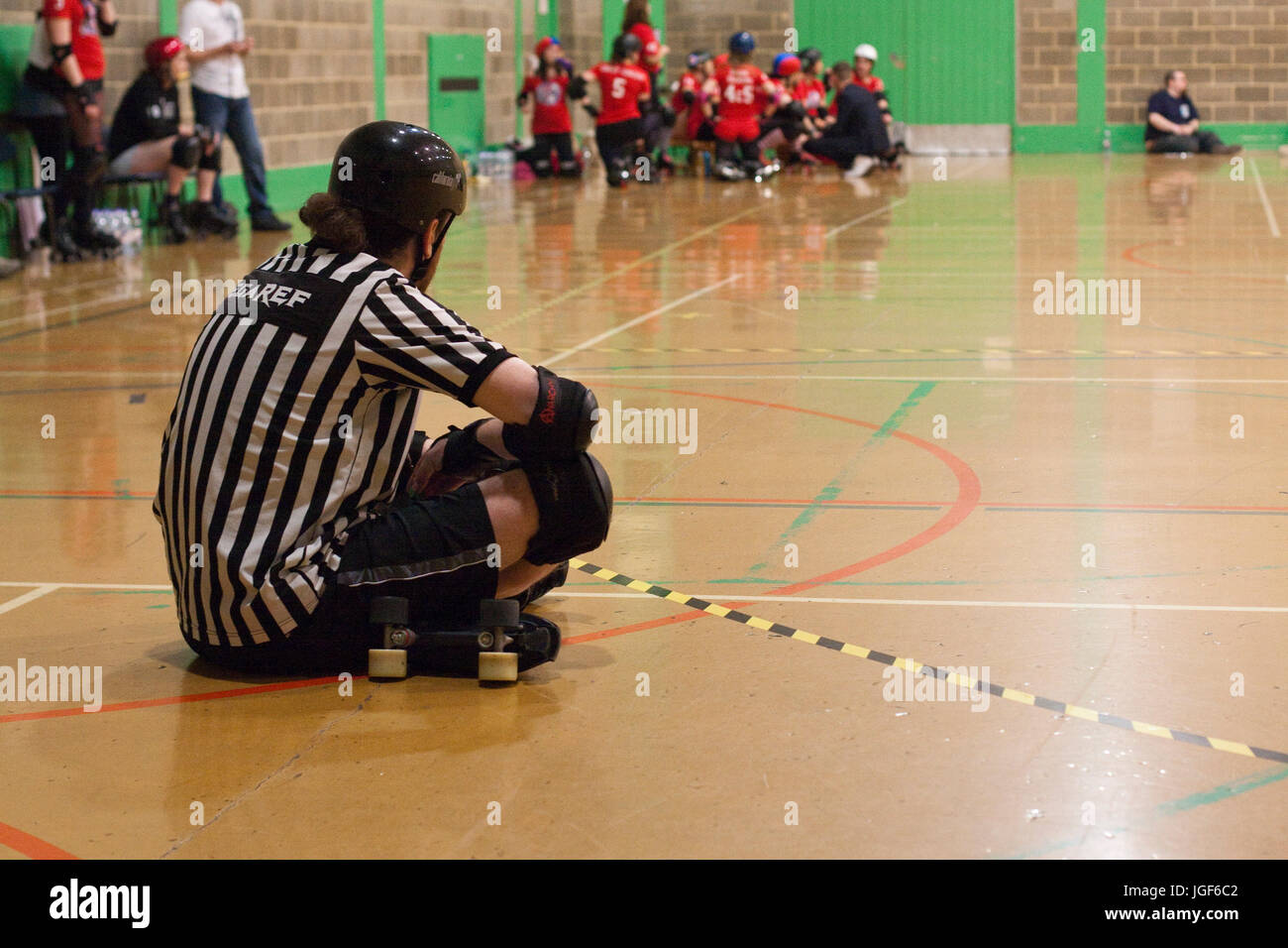 Male roller derby ref sits crosslegged by the track waiting for a bout ...