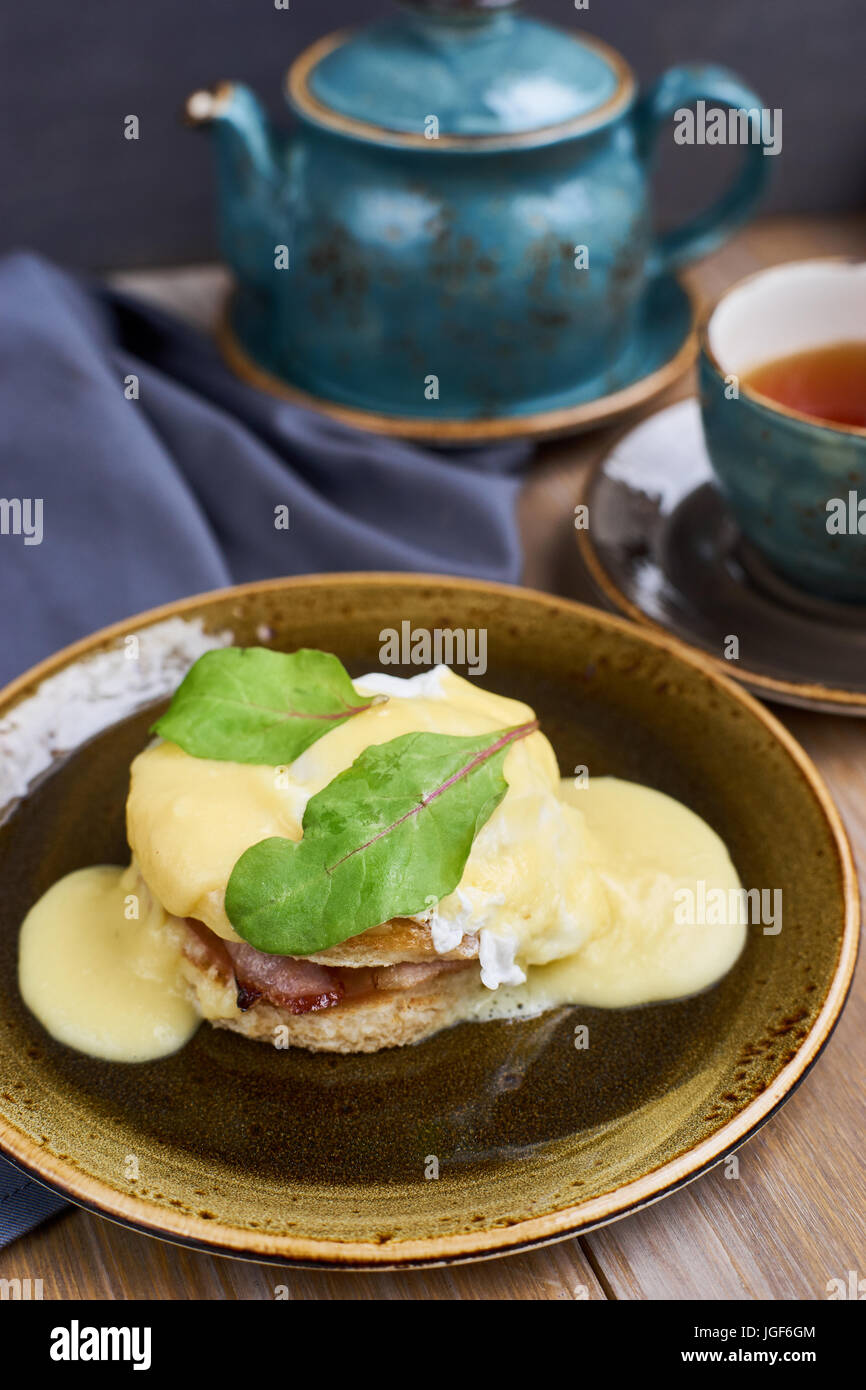 Breakfast. Delicious eggs benedict served on plate. Teapot and cup of ...
