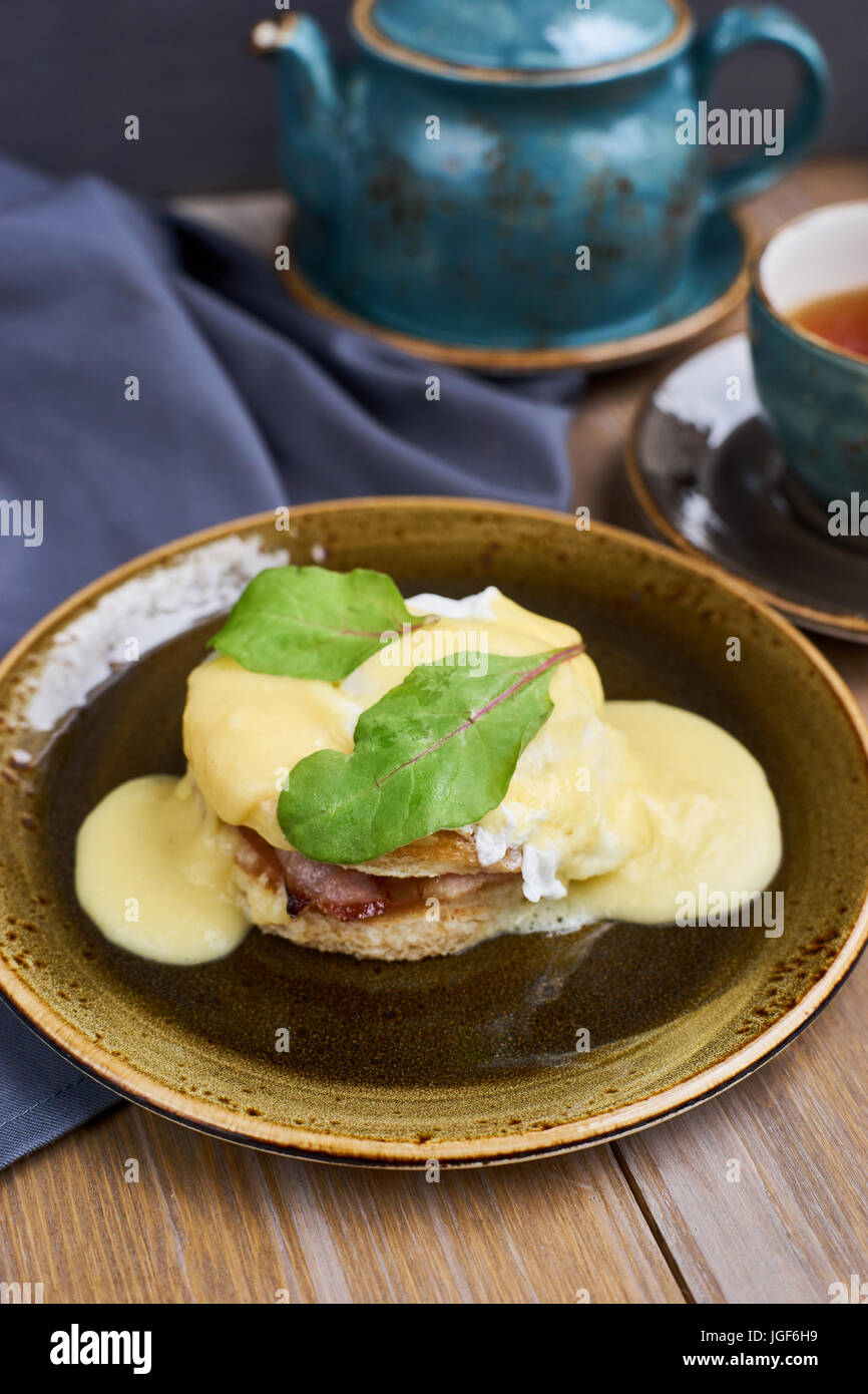 Breakfast. Delicious eggs benedict served on plate. Teapot and cup of ...