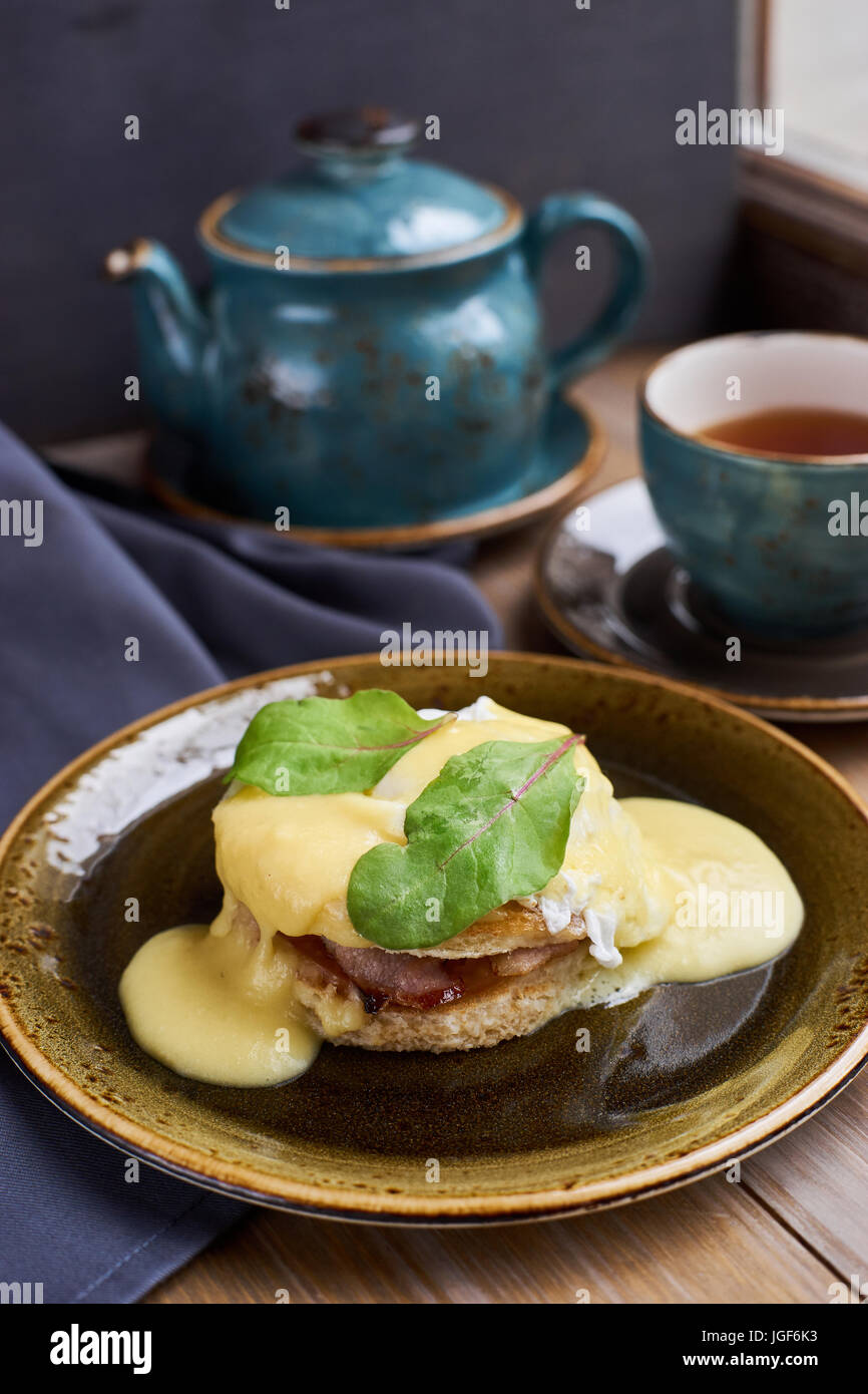 Breakfast. Delicious eggs benedict served on plate. Teapot and cup of ...