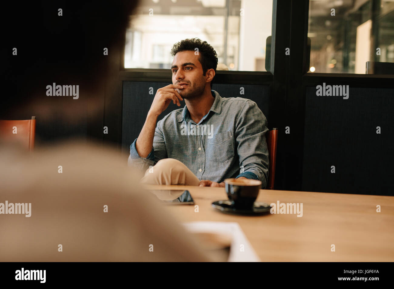 Handsome young man sitting at table in conference room and listening to ...