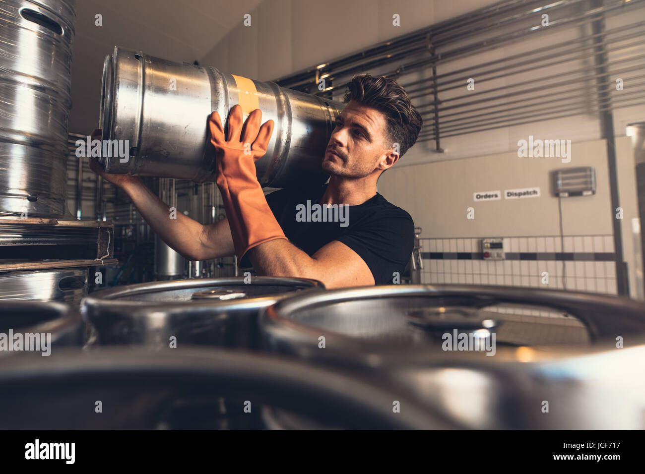 Brewer carrying metal beer barrel at brewery factory. Young man working ...