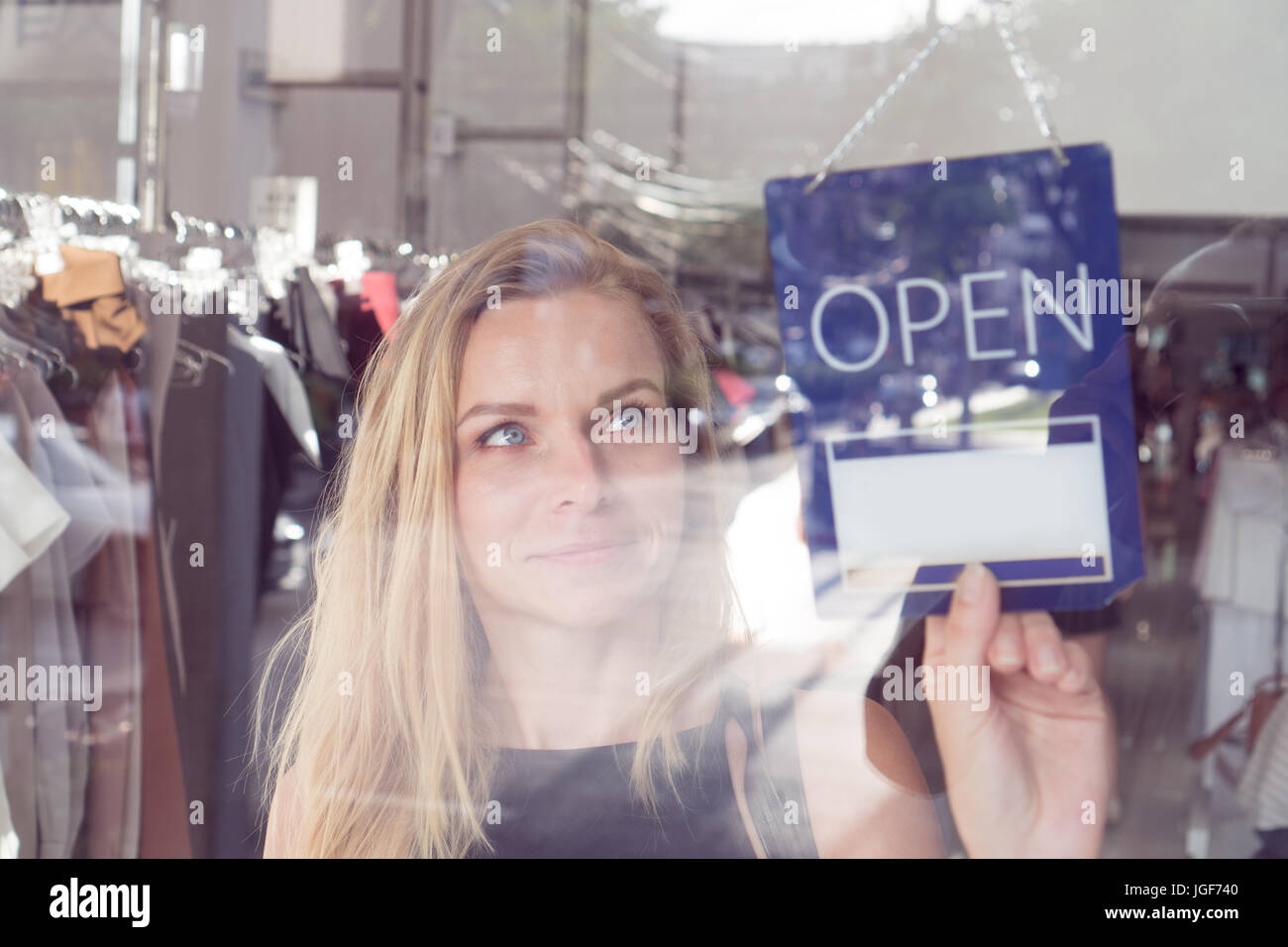 Pretty blond woman turning the open and closed sign in clothes shop ...