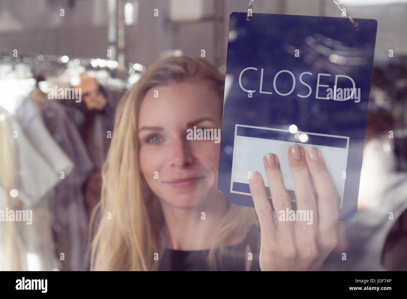 Pretty blond woman turning the open and closed sign in clothes shop ...