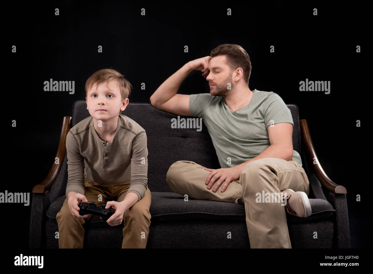 Upset father sitting on sofa near little son playing with joystick ...