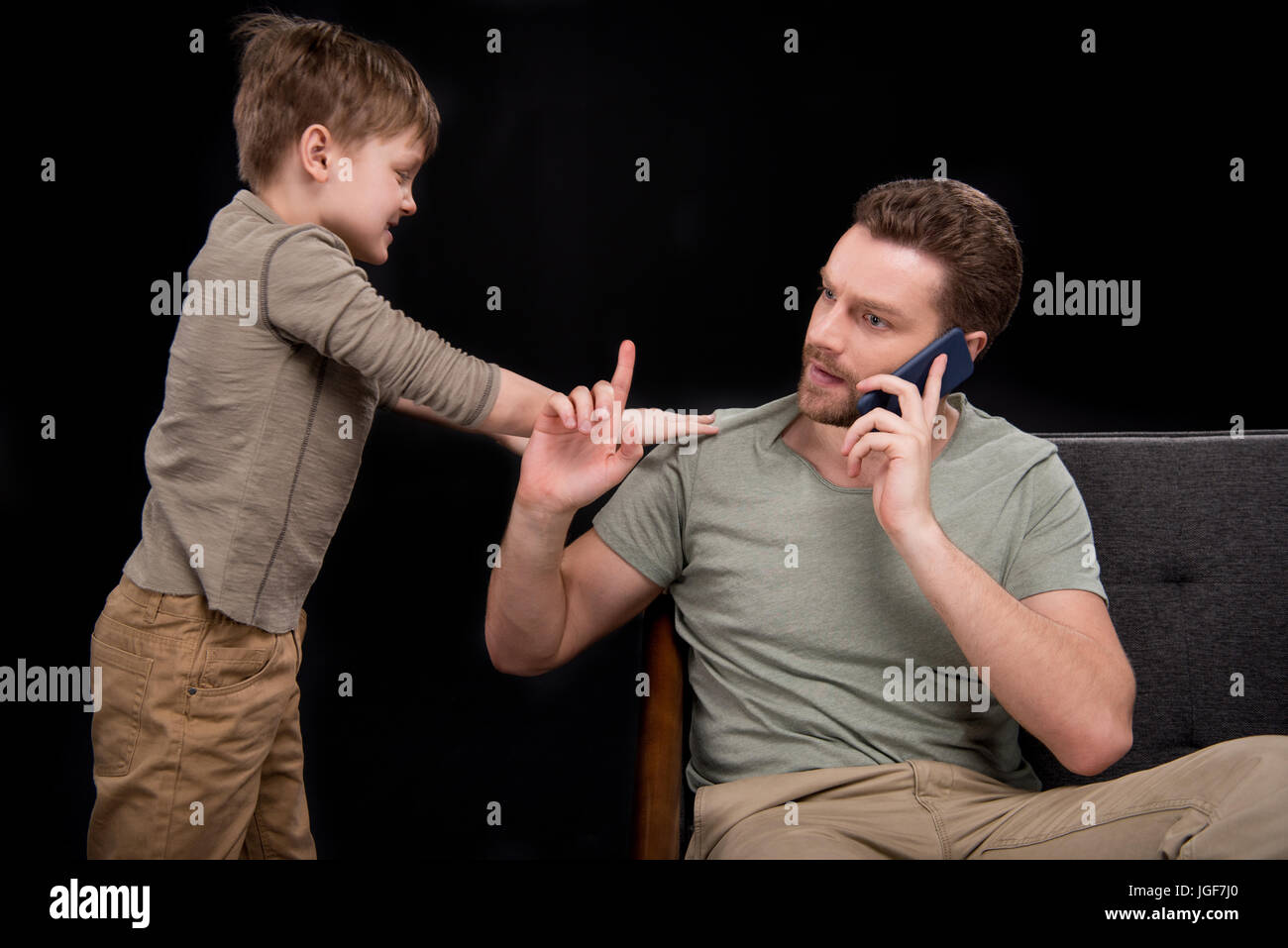 Upset little boy trying to talk with father talking on smartphone ...
