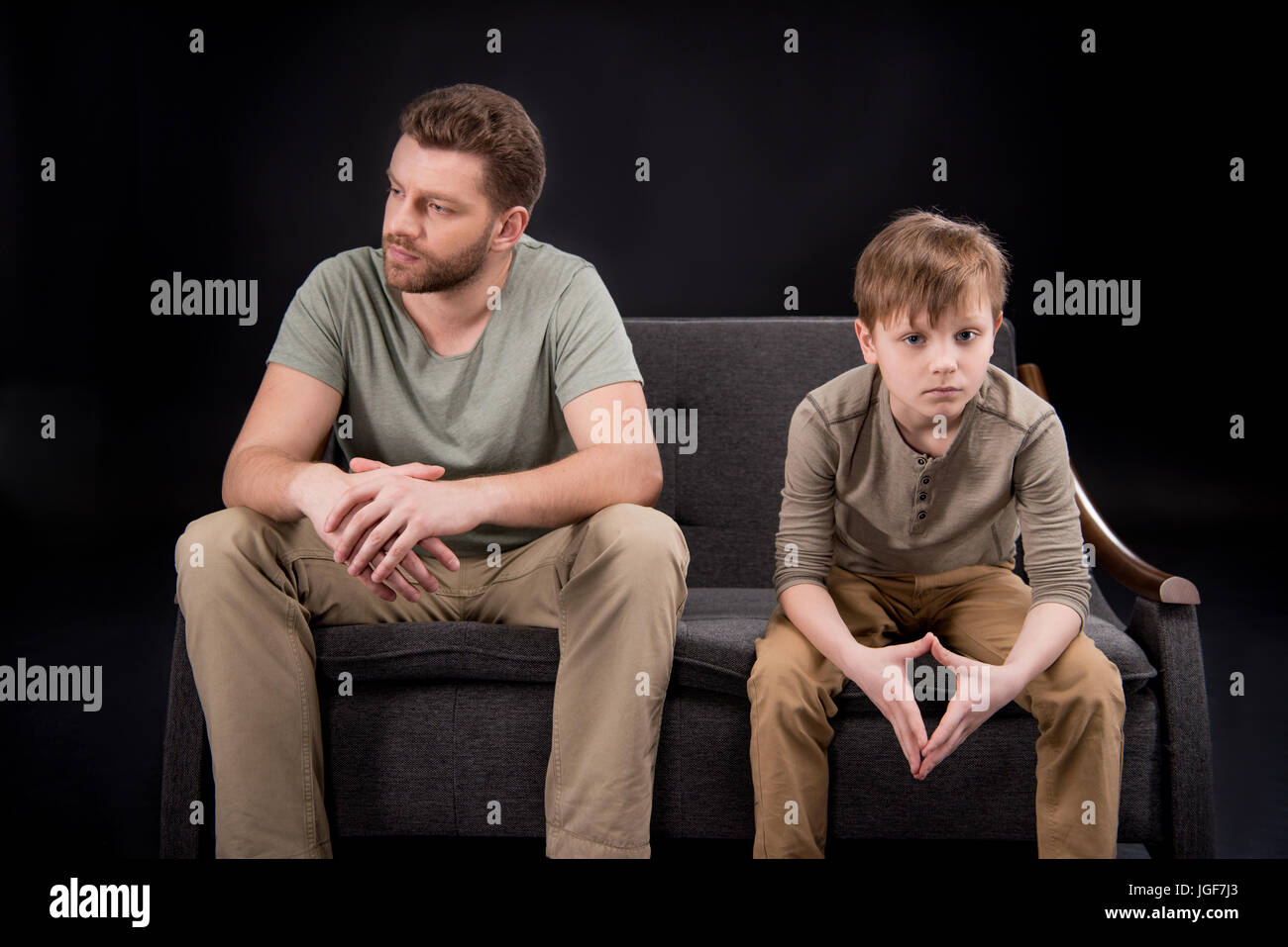 Upset father and son sitting on sofa and looking away, family problems ...