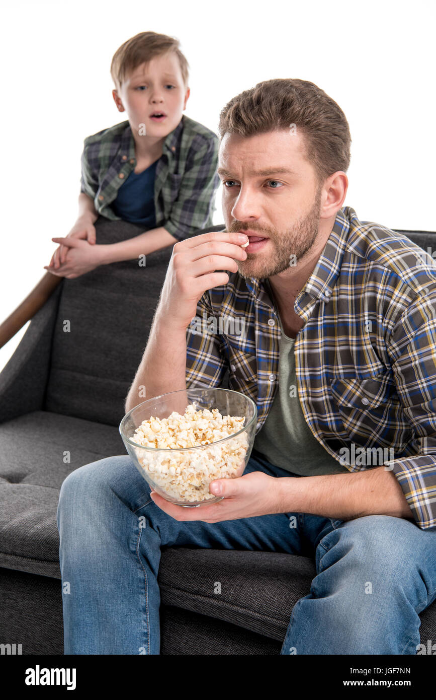 Son talking with father sitting on sofa and eating popcorn from bowl ...