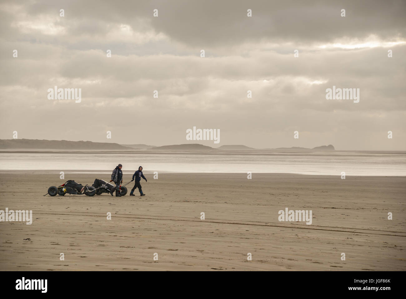 Two people pulling sand yachts on Welsh beach following strong winds ...
