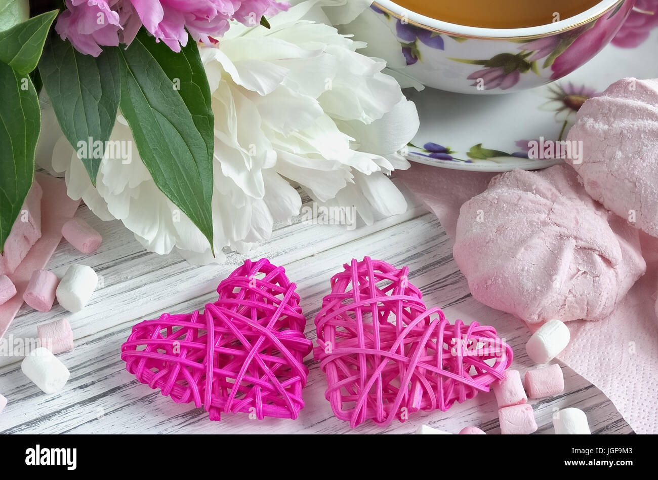 Peonies flowers pink cup of tea rattan hearts marshmallow on a white wooden background - stock ...