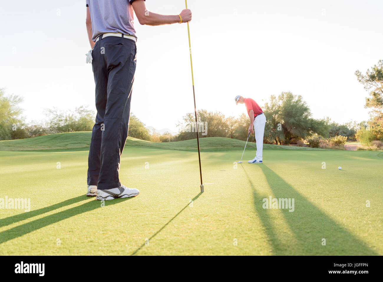 Hispanic man watching friend on golf course Stock Photo - Alamy