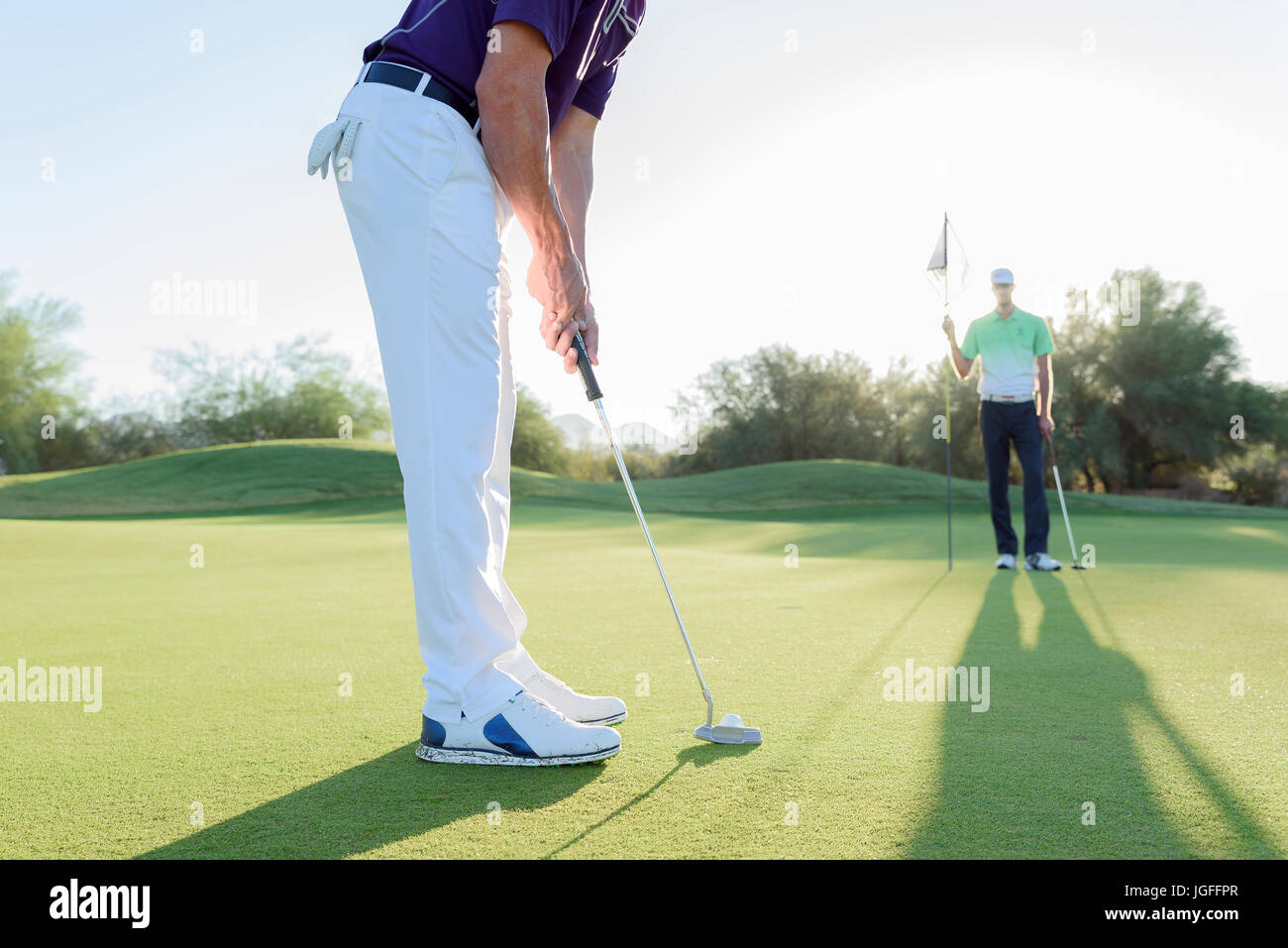 Hispanic man watching friend putting on golf course Stock Photo - Alamy