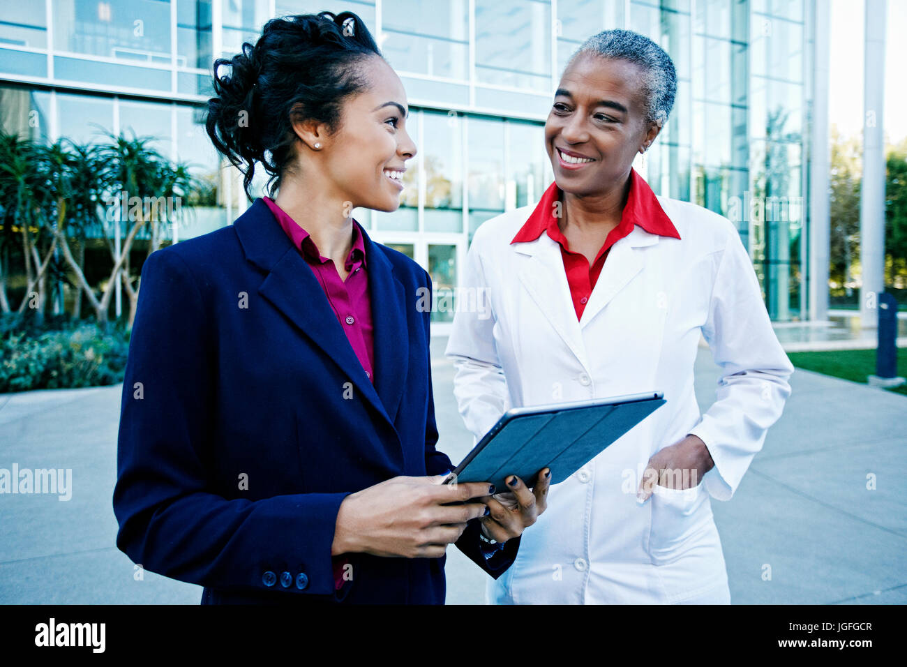 Doctor and administrator outdoors at hospital using digital tablet ...