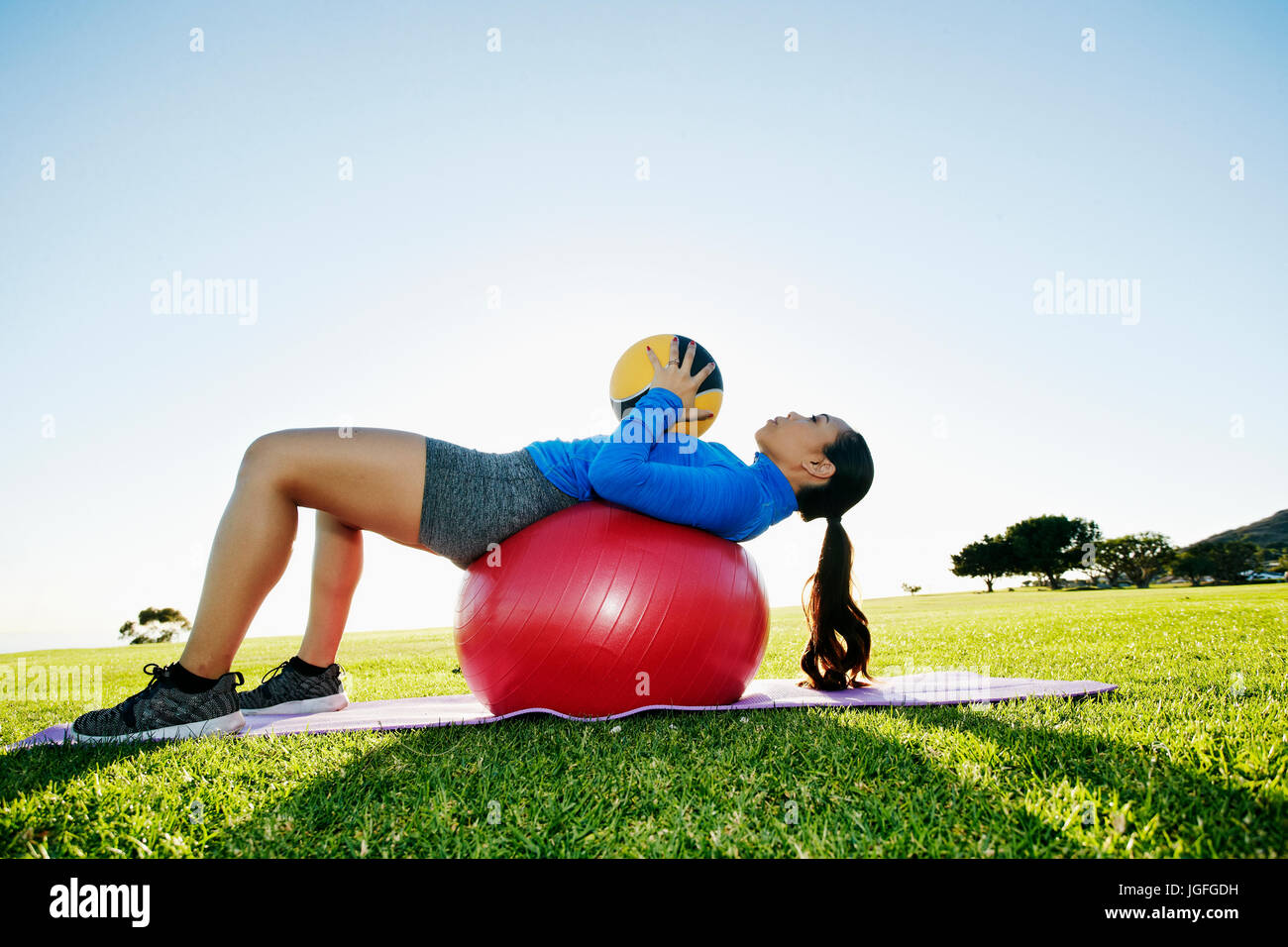 Mixed Race woman exercising with fitness ball and heavy ball in sunny ...