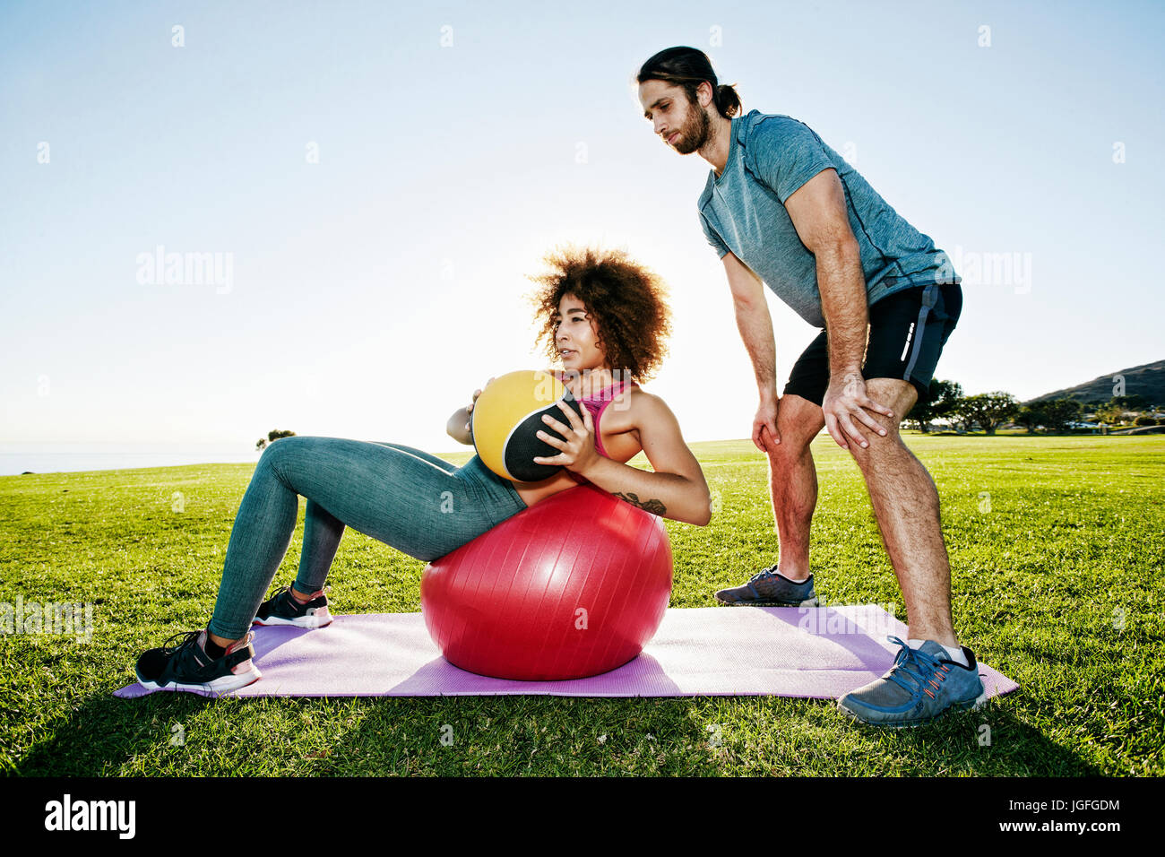 Couple exercising with fitness ball and heavy ball in sunny field Stock ...