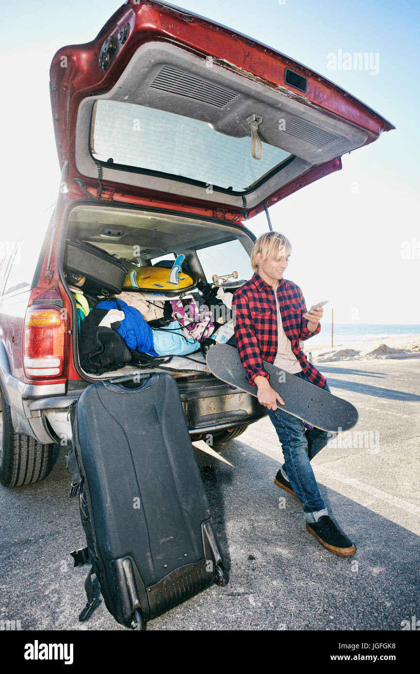 Caucasian man holding skateboard and texting on cell phone Stock Photo ...
