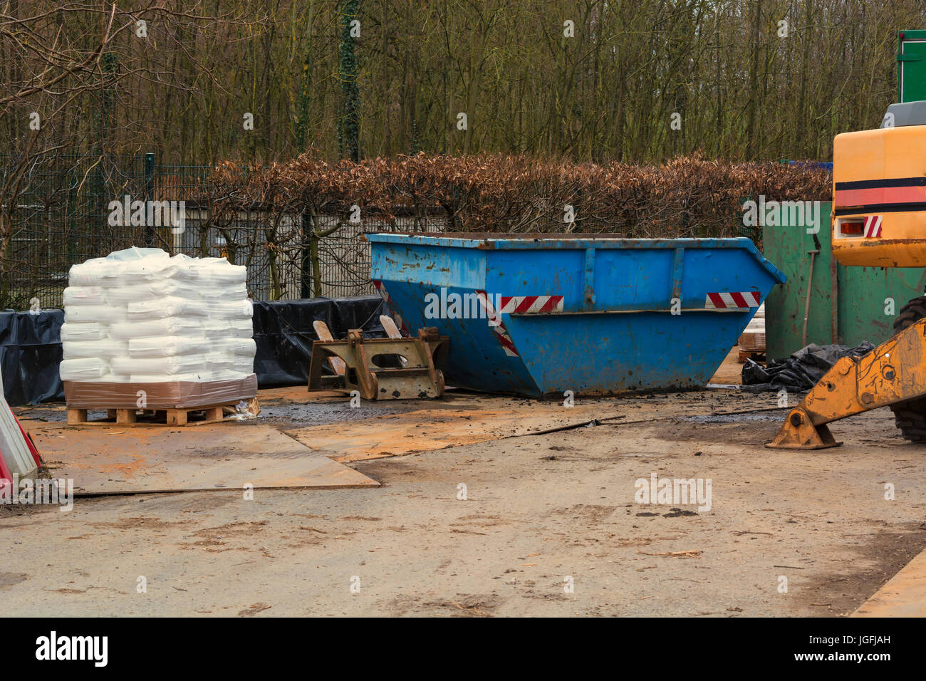 Blue container an excavator and pallet with white bags on a ...